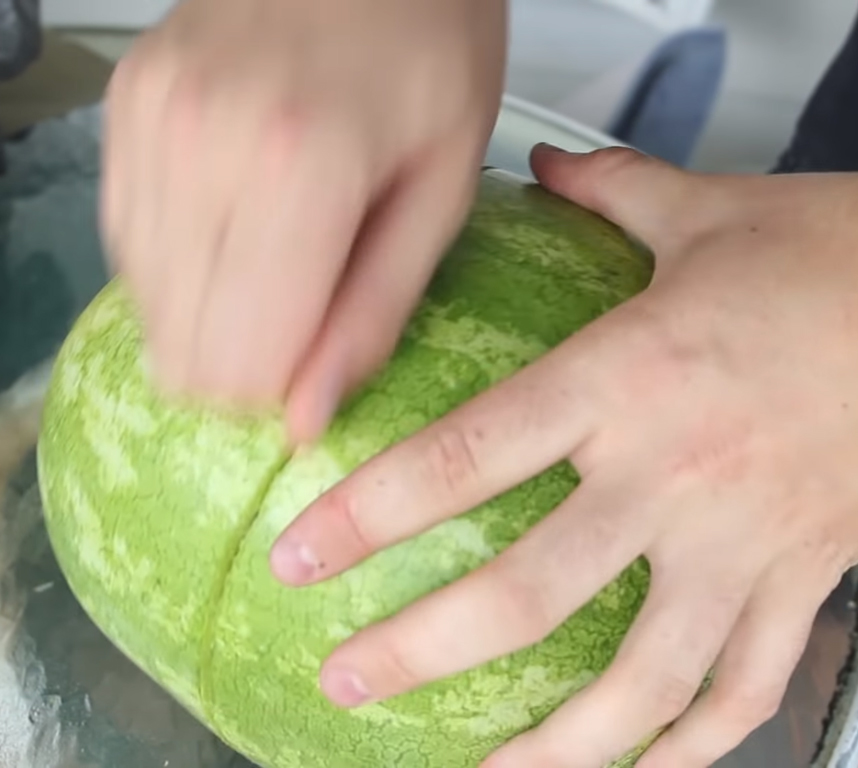 Guy demonstrates how to open up a watermelon using just a quarter